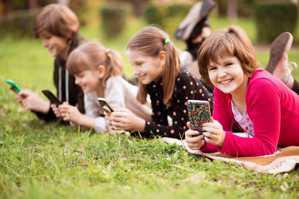 Outdoor portrait of little girl with friends playing with phones ...